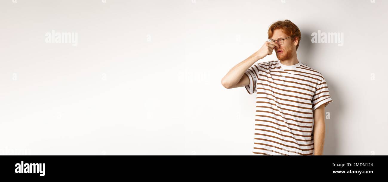 Young man with red hair staring at camera and shut nose from bad smell ...