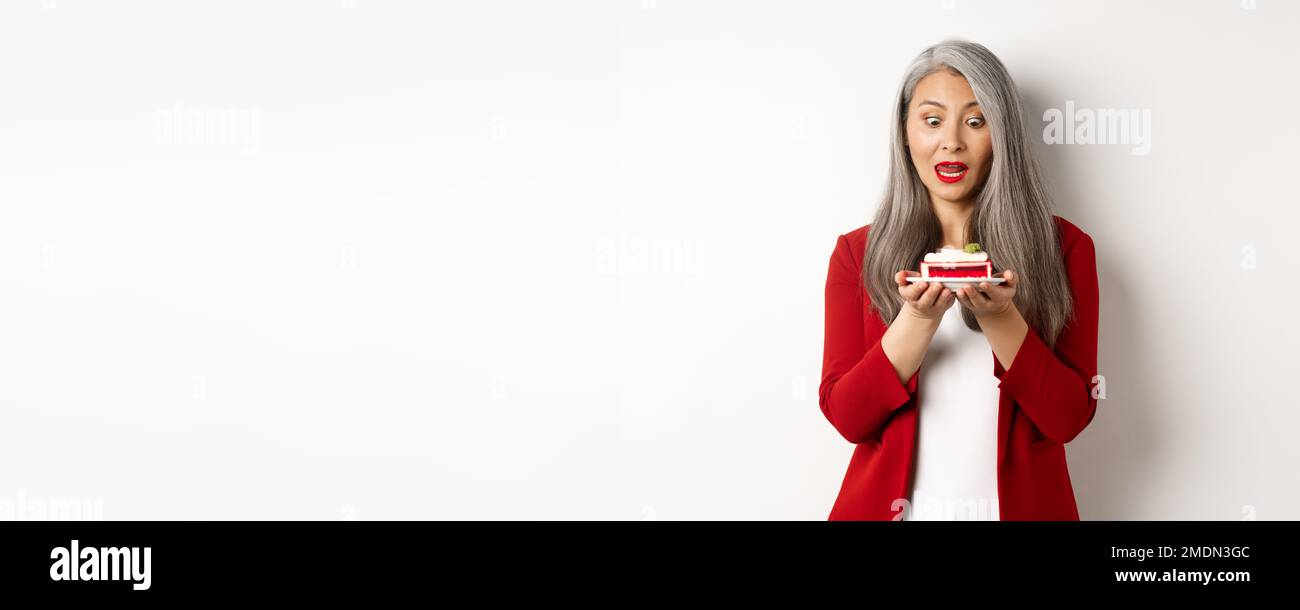 Image of funny asian senior woman looking tempted at piece of cake ...
