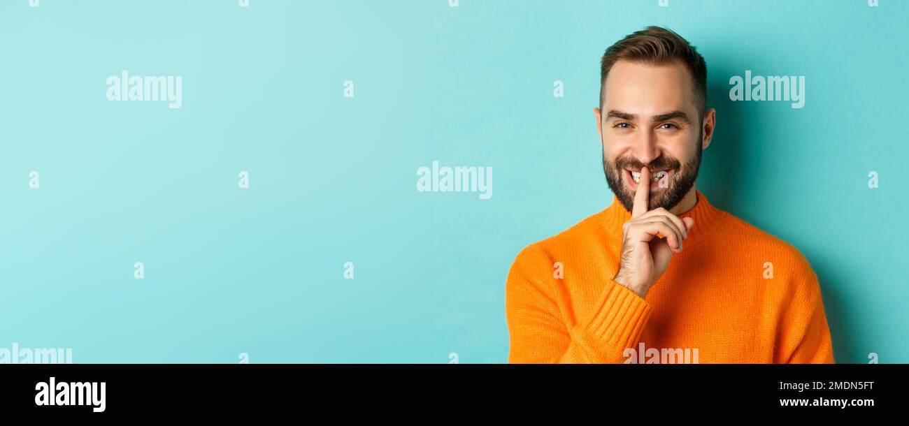 Close-up of handsome smiling man hushing, telling secret, standing over ...