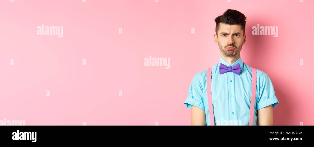 Sad and offended young man, frowning and pucker lips, looking angry at ...