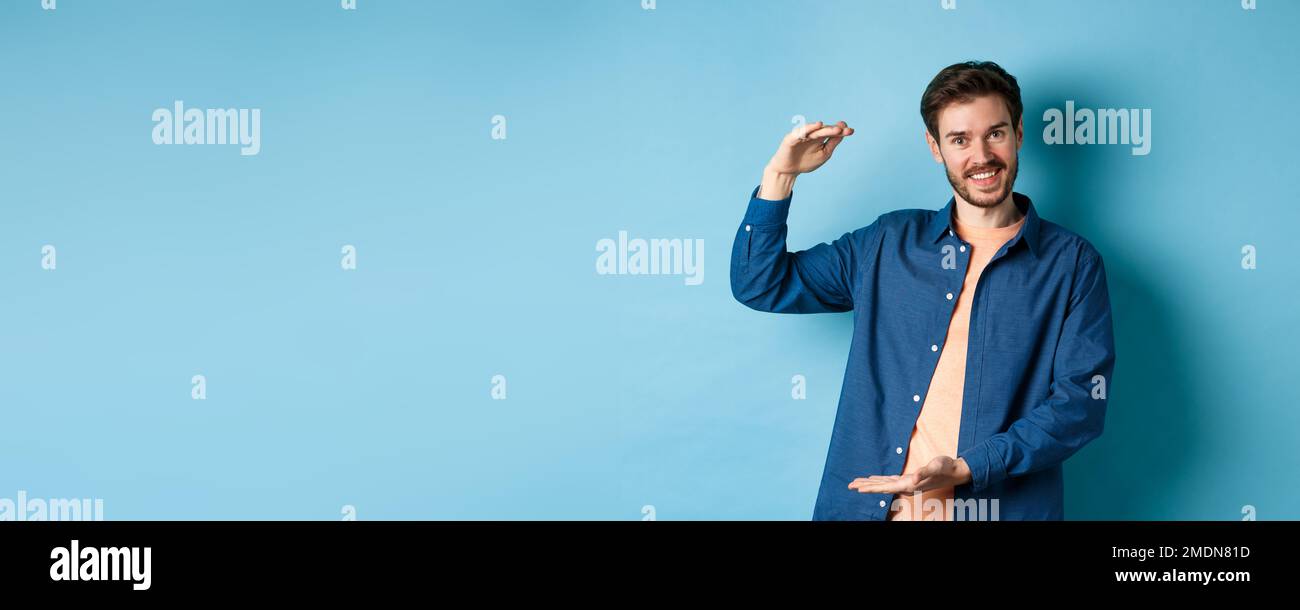 Handsome caucasian guy showing something big, shaping large size object ...