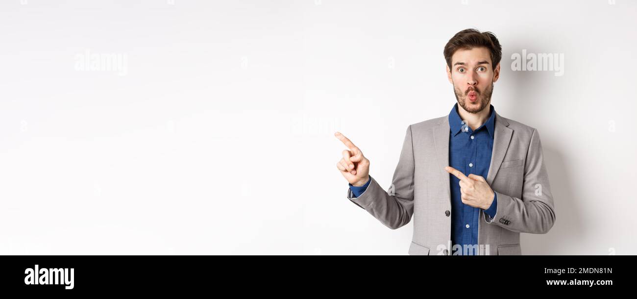 Excited handsome man in suit pointing fingers left at banner and saying ...