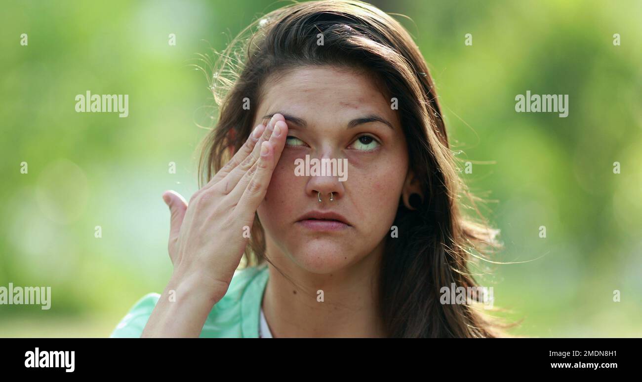 Woman looking to camera adjusting and rubbing face with hand, grimacing ...