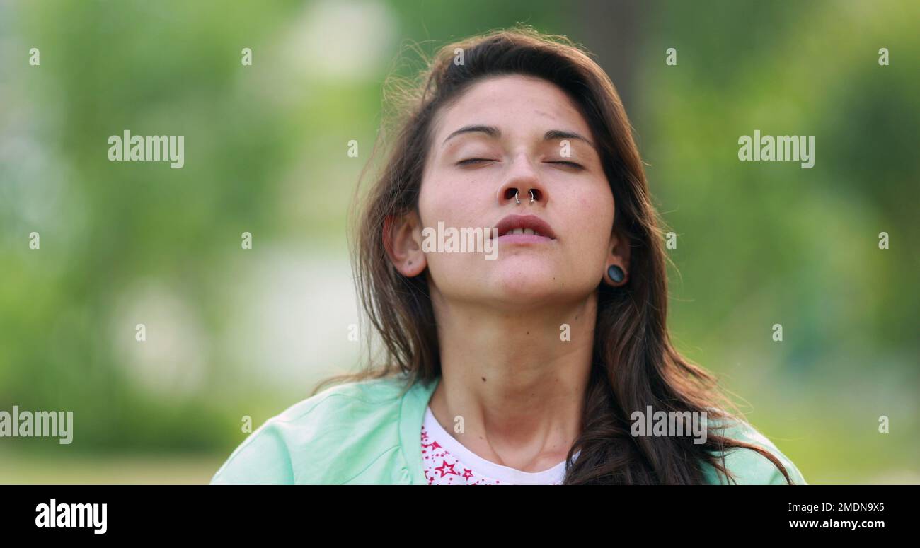 Young woman taking a deep breath outdoors feeling relaxed and happy at ...
