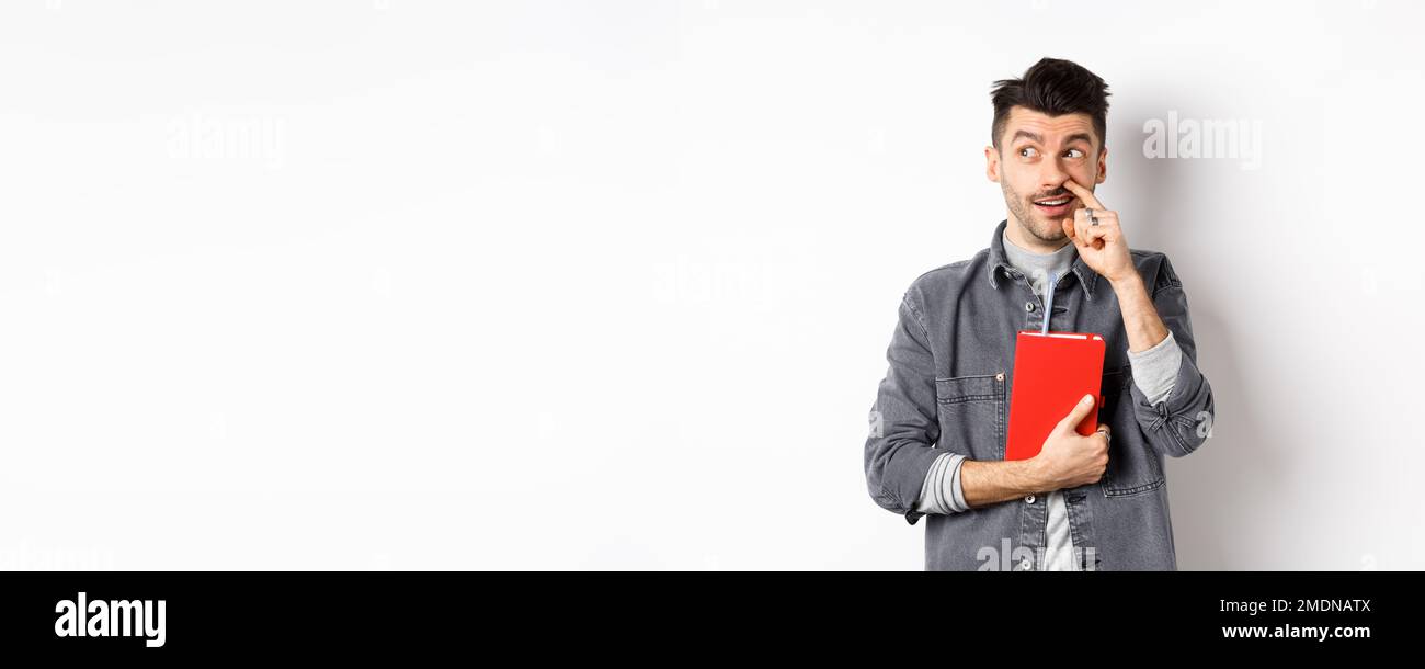 Guy picking nose and look aside at logo, holding red book or planner in ...