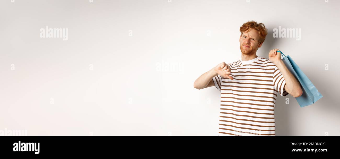 Disappointed young man with red hair and beard showing thumbs-down ...