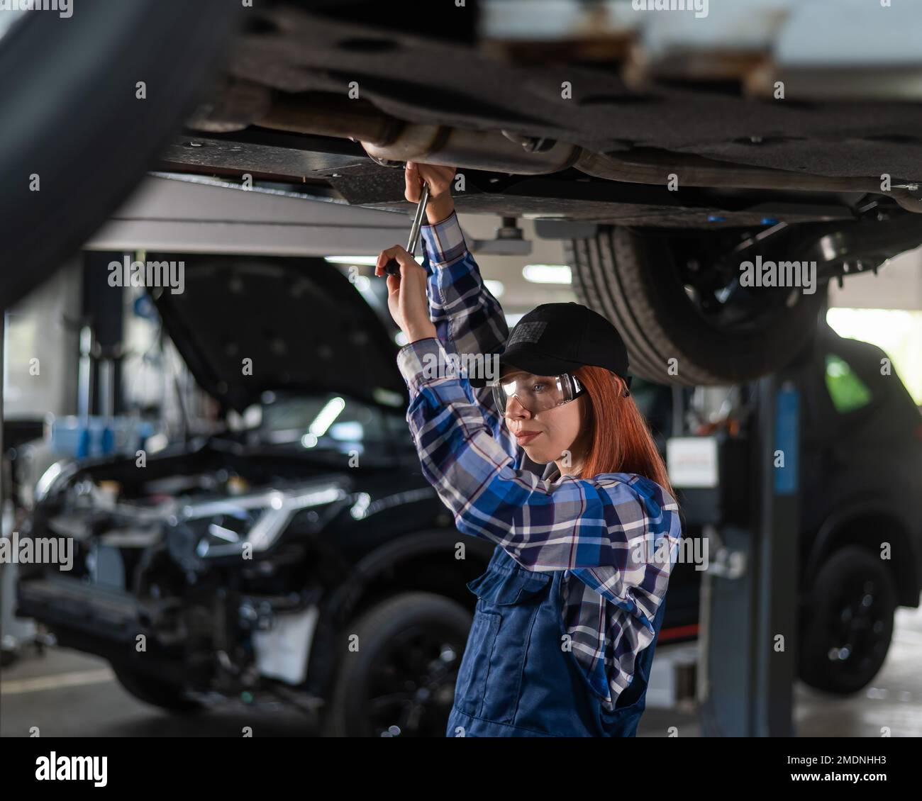 Female mechanic unscrew the nuts on the bottom of the car that is on ...