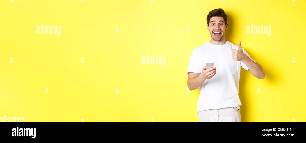 Happy smiling man holding smartphone, showing thumb up in approval ...