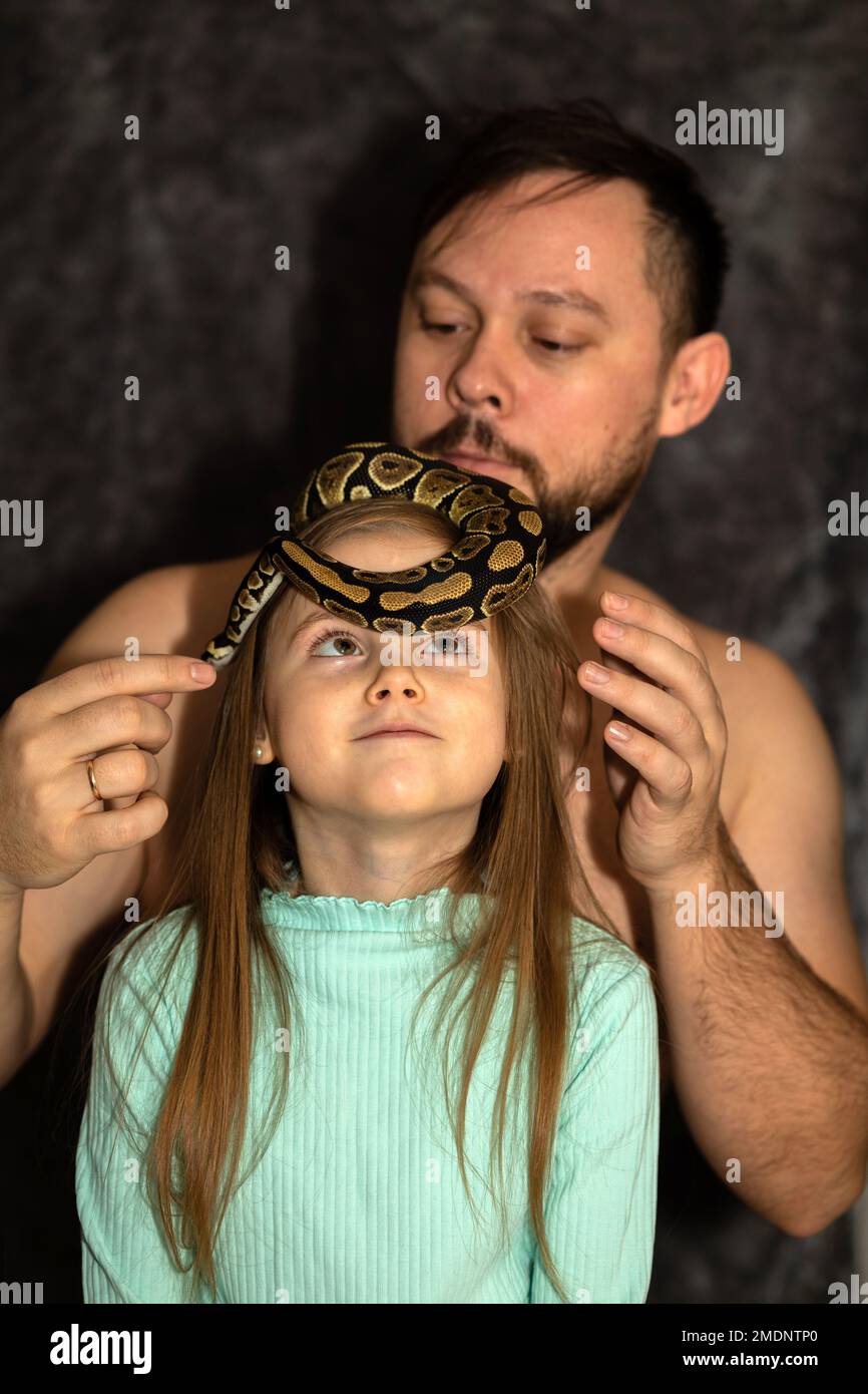 Father and daughter playing with snake. Portrait of smiling girl in ...