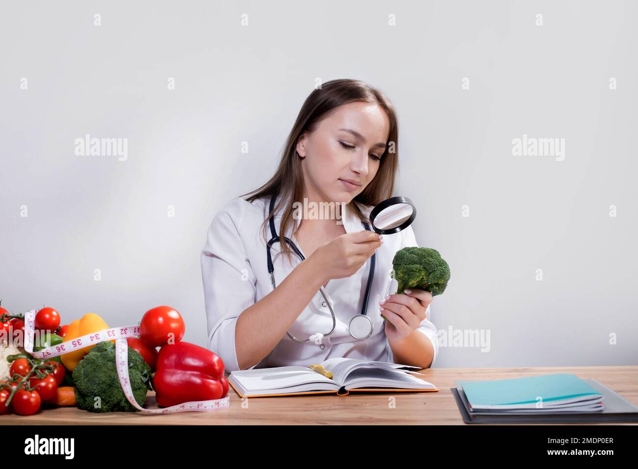A female nutritionist looks through a magnifying glass at broccoli in ...