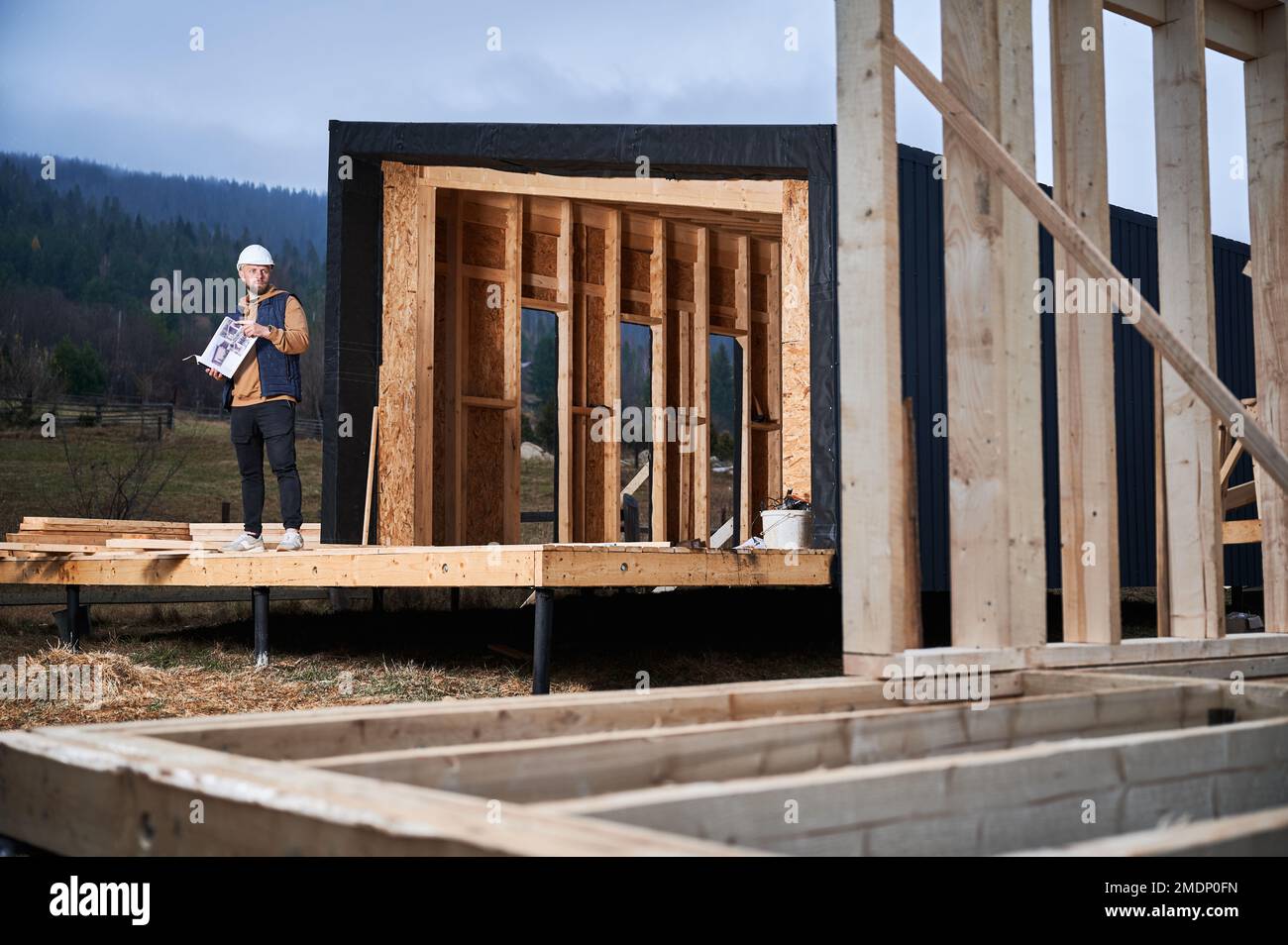 Male engineer building wooden frame house on pile foundation. Man builder standing on ...