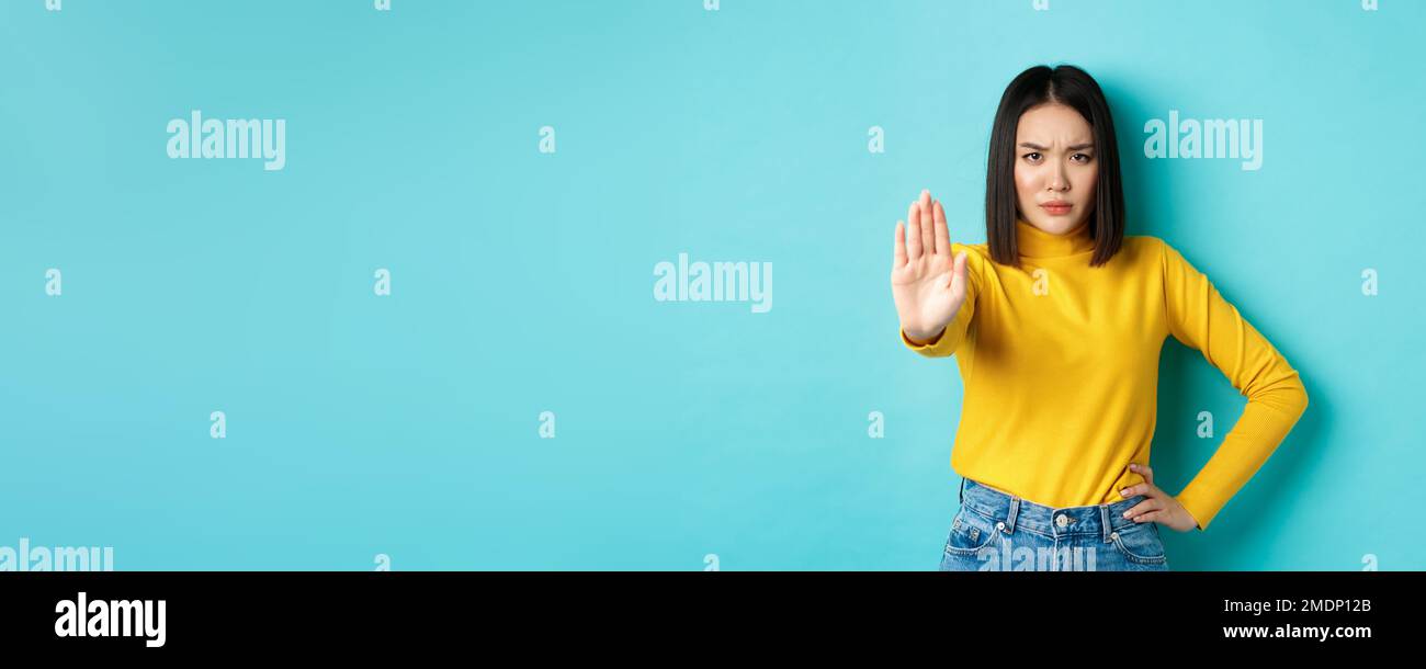 Confident and serious asian woman tell no, showing stop gesture to ...