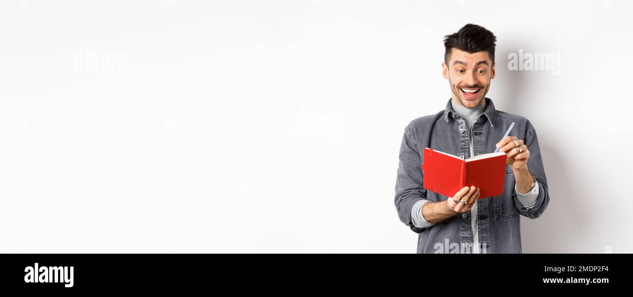 Excited guy writing in planner and smiling, writing down ideas in ...