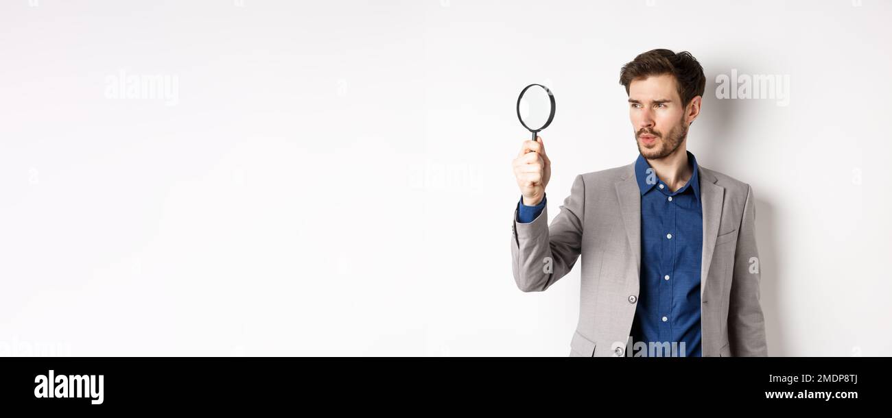 Serious man in suit searching for clues through magnifying glass ...