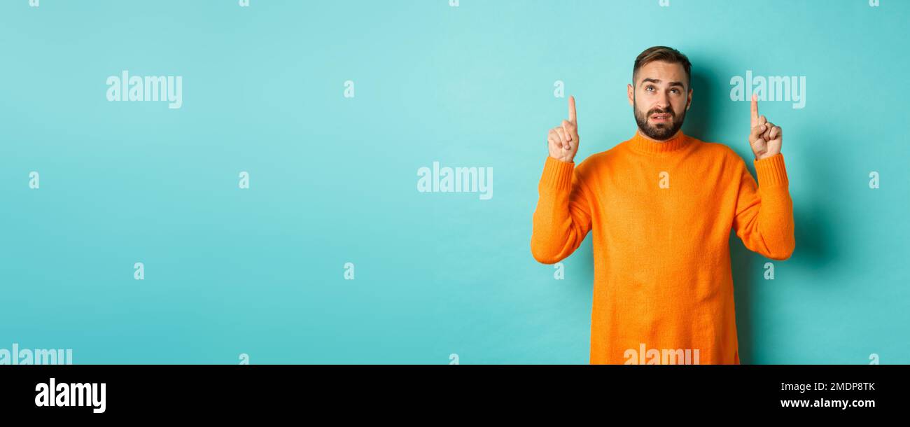 Doubtful and unamused man looking, pointing fingers up something ...