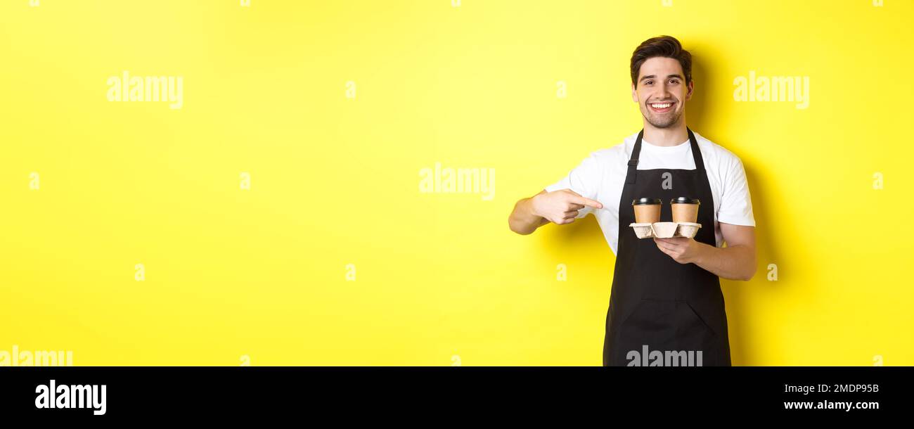 Handsome barista holding two cups of takeaway coffee, pointing finger ...