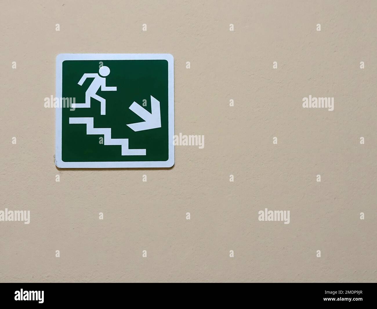 Green sign down the stairs on a bright wall. Direction to the emergency ...