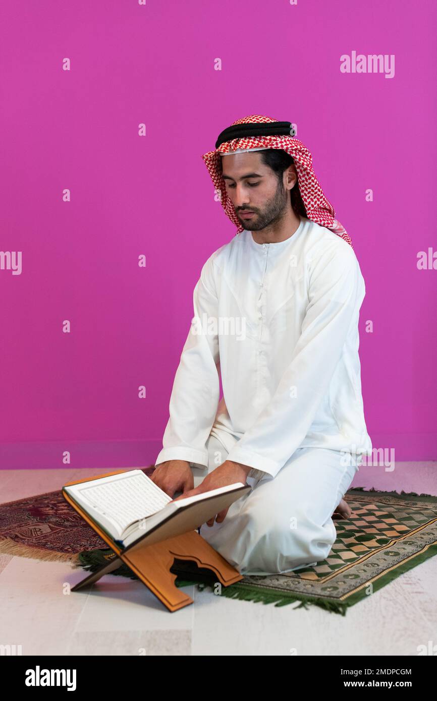 Young arabian muslim man in traditional clothes reading holy book Quran ...