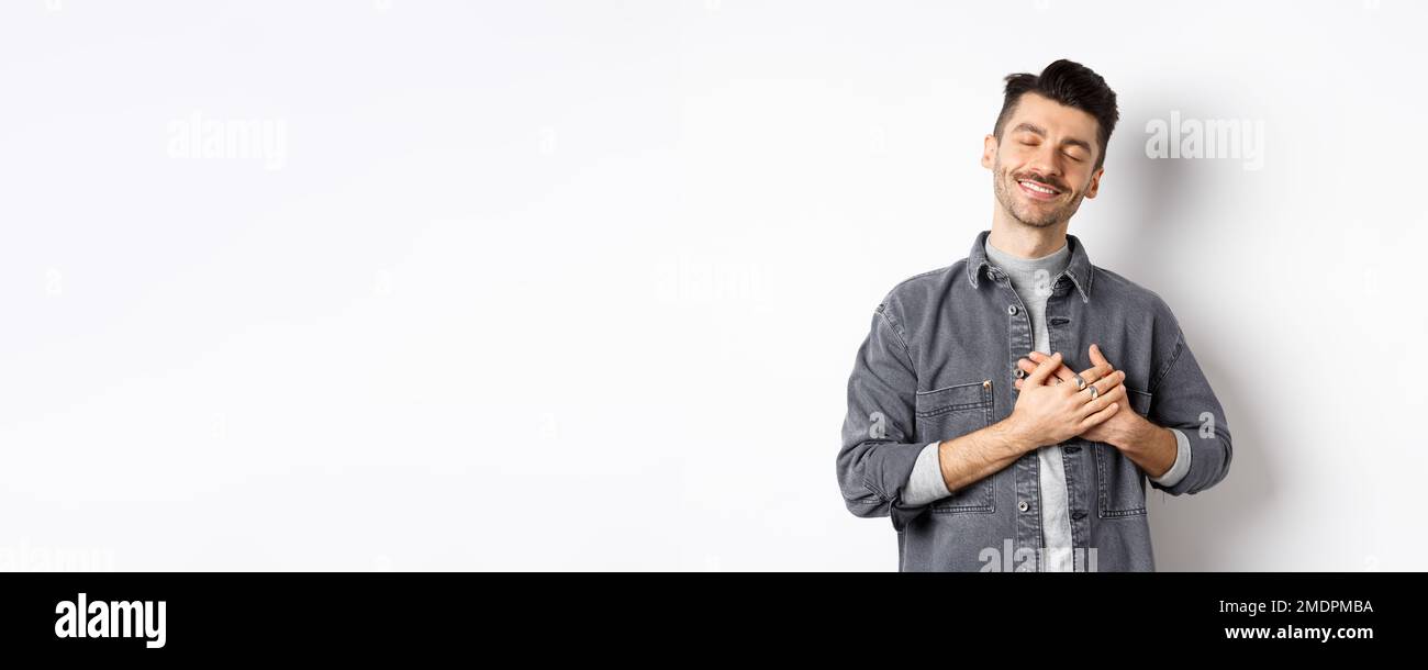 Romantic happy man holding hands on heart and smiling with closed eyes ...
