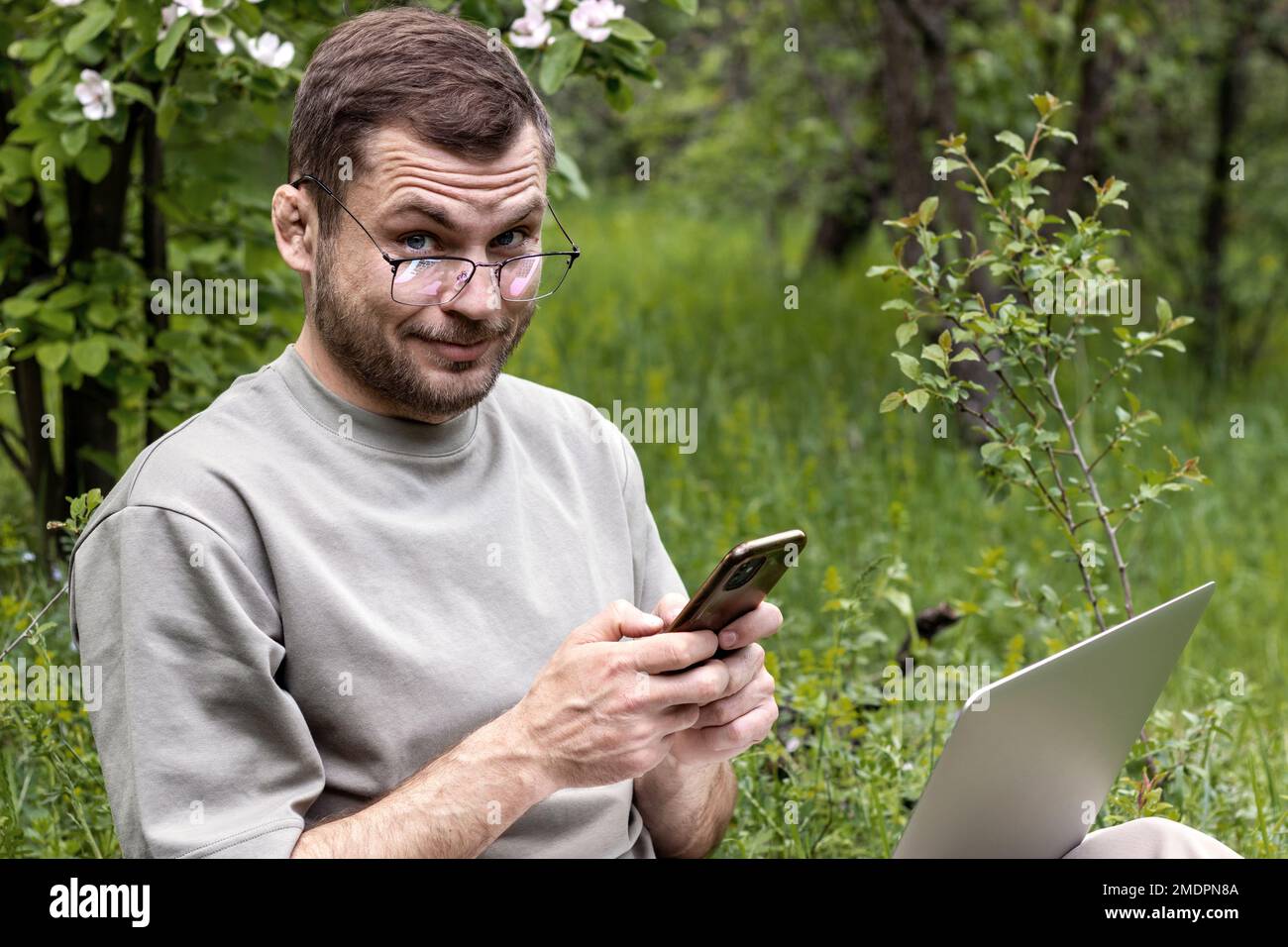 Man with cunning eyes wearing glasses uses his cell phone and laptop ...