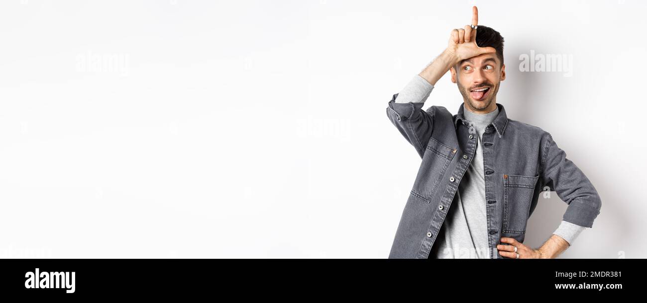 Funny guy mocking person, showing tongue and loser sign on forehead ...