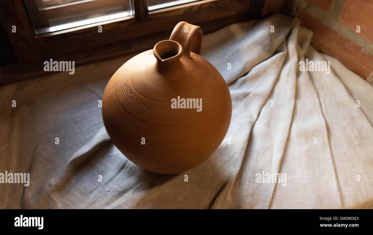 Ancient pottery stands on the window sill. Brown earthenware jug ...