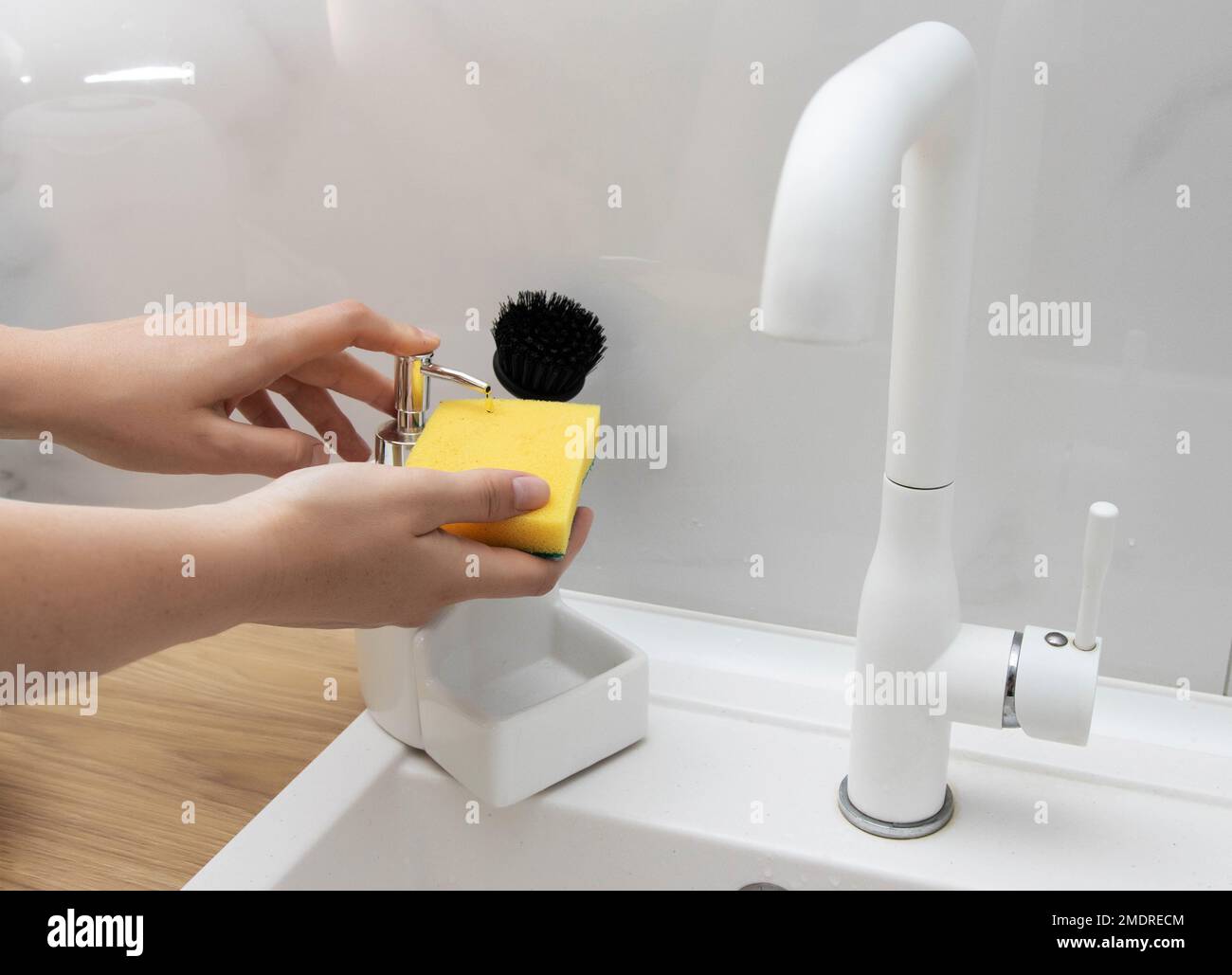 A girl applies an anti-grease detergent to a dishwashing sponge. White ...