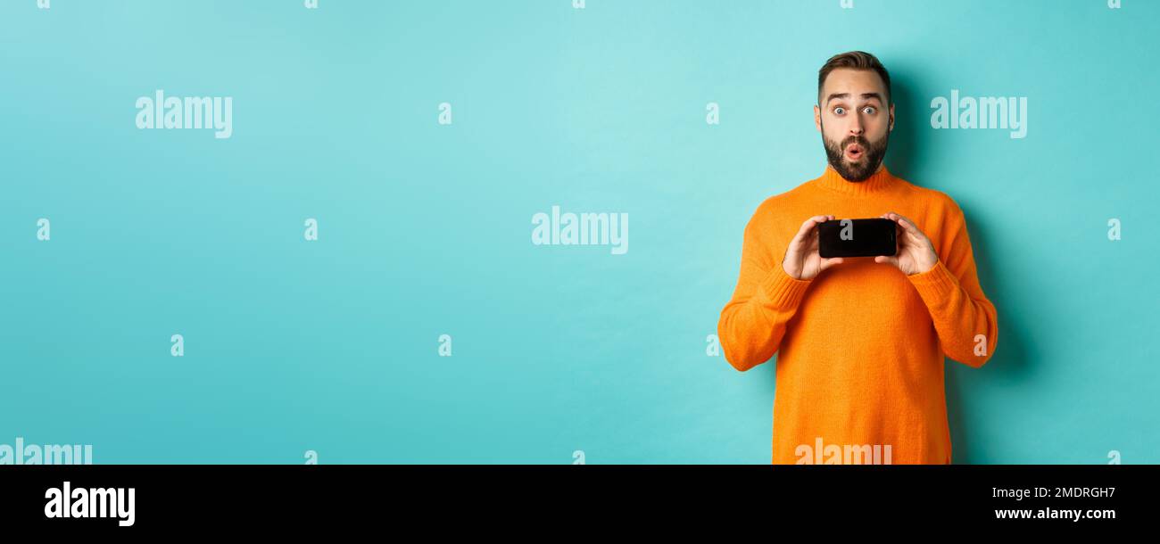 Impressed man showing smartphone screen, stare at camera amazed ...