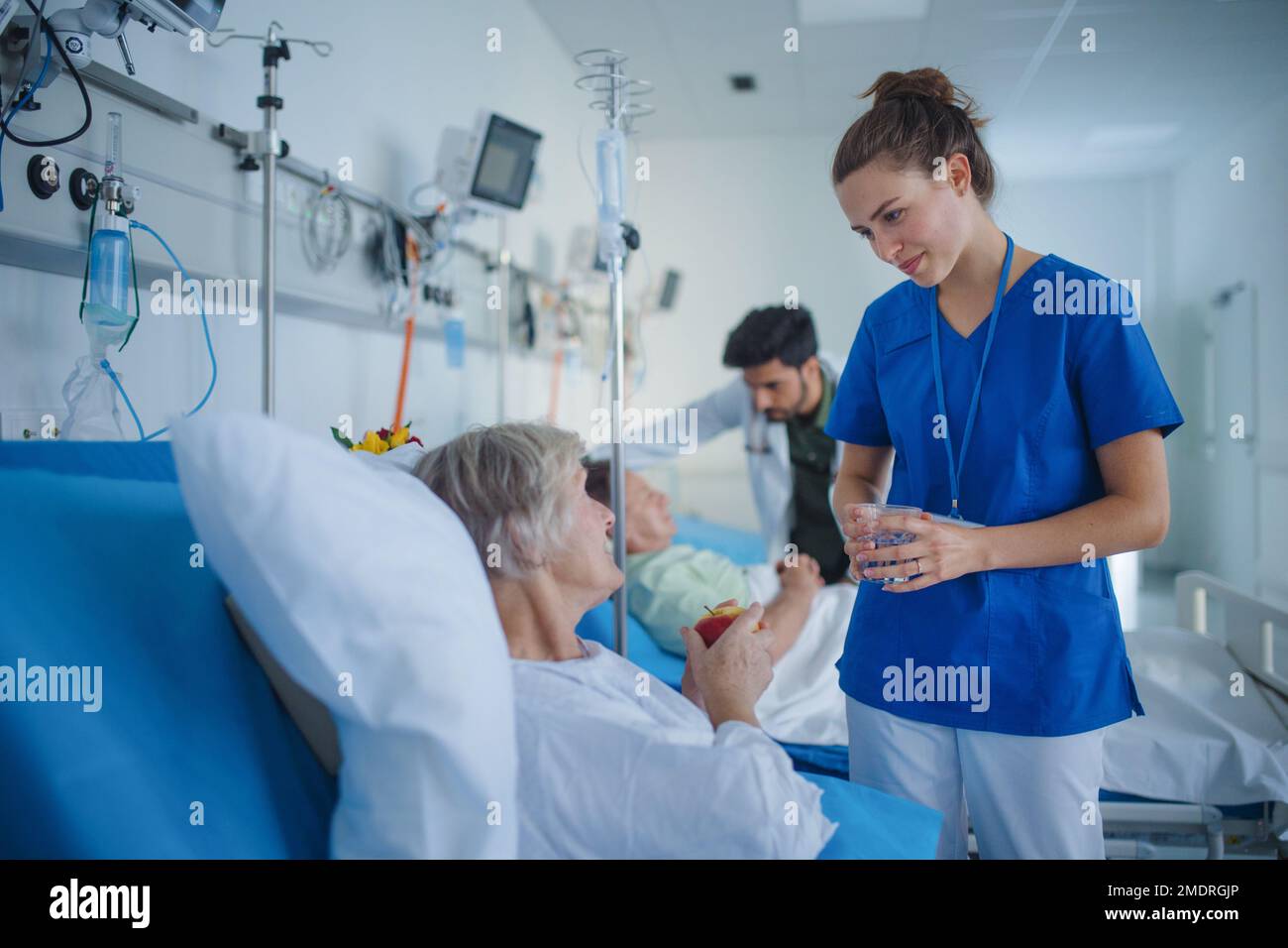 Young nurse giving glass of water to senior patient at hospital ward ...