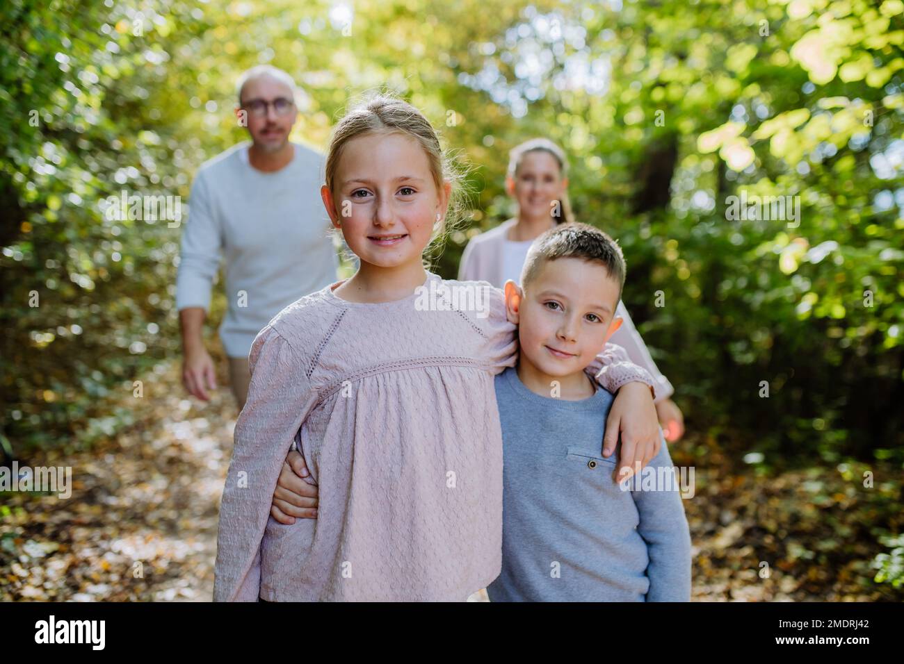 Portrait of little children, siblings, hugging in forest, their parent ...