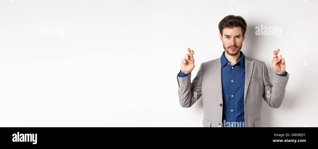 Hopeful man in suit cross fingers for good luck and looking confident ...
