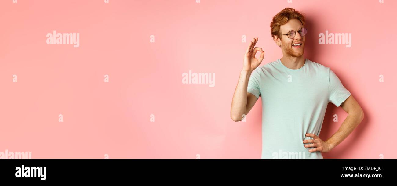 Cheerful guy with red hair and beard, wearing glasses, showing OK sign ...