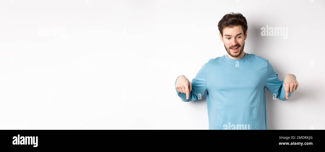 Handsome caucasian man pointing down with impressed and happy face ...