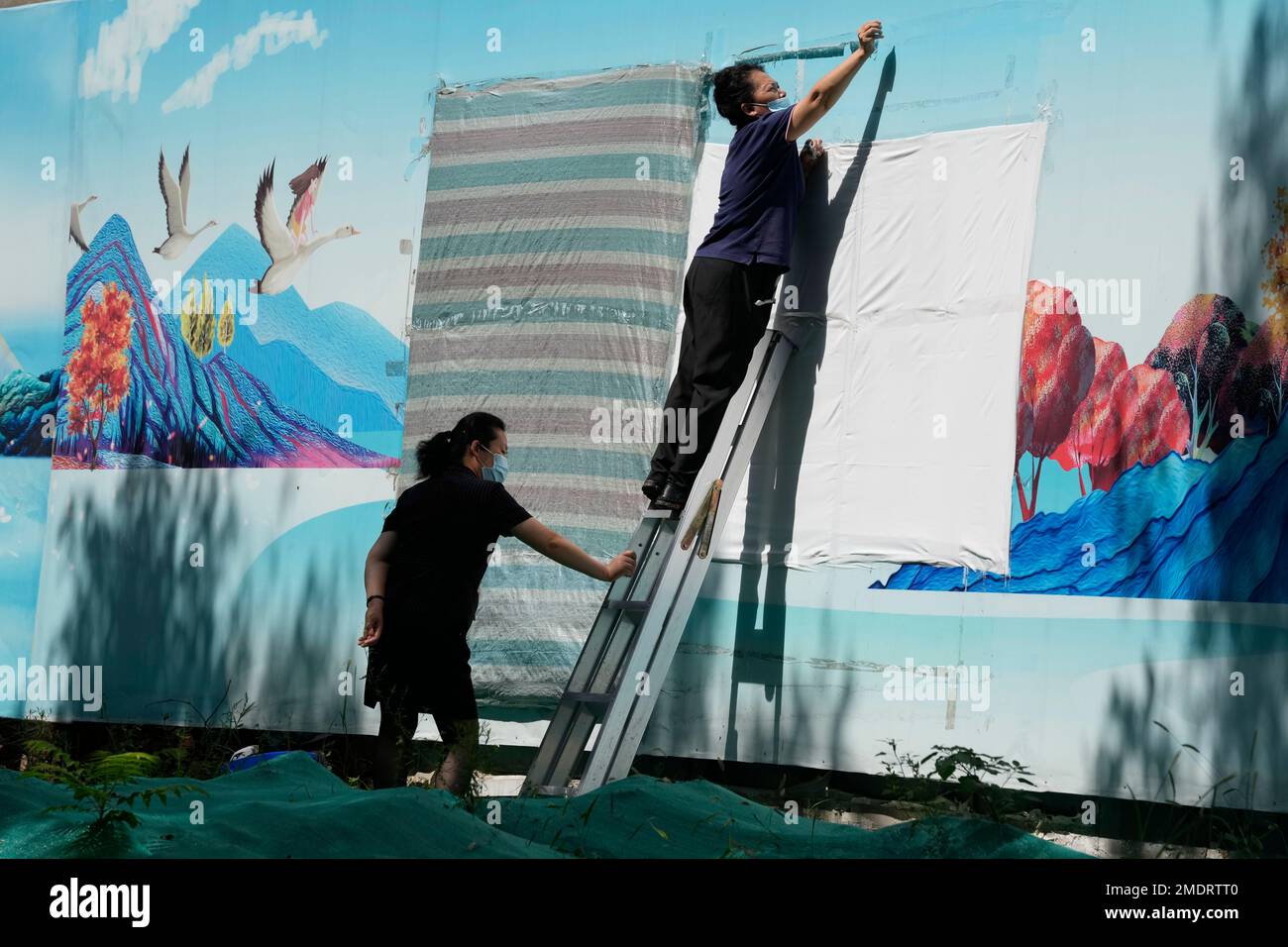Workers clean up stains on a mural around a building under renovation ...