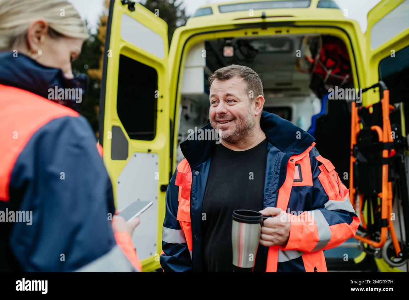 Rescuers having break in front of ambulance car, talking and drinking ...