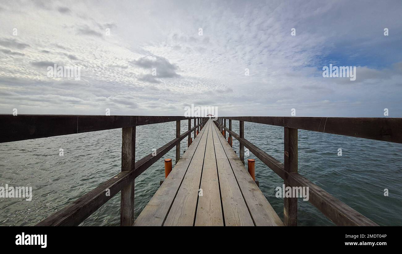 A wooden pier extending into the ocean with clouds in the sky Stock ...