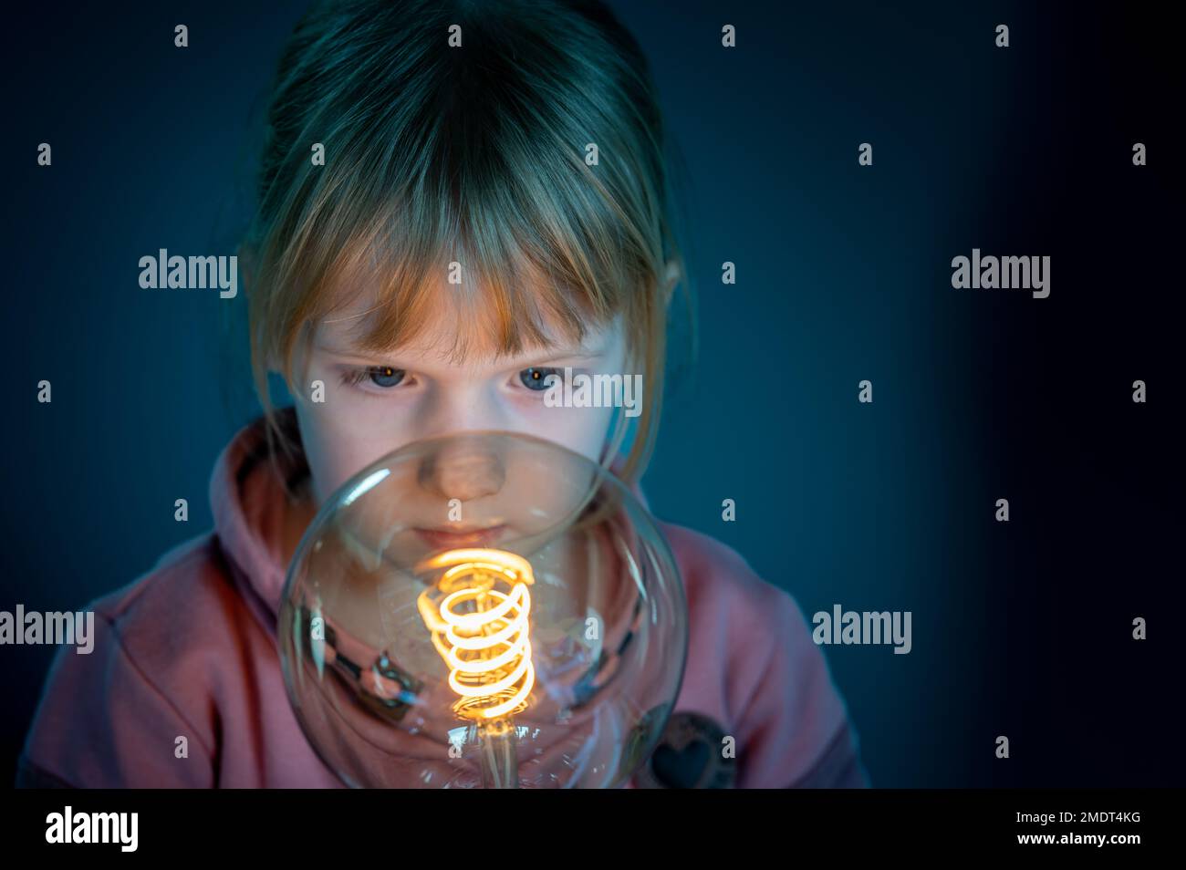 Young child looks concentrated through a filament light bulb. Symbol ...