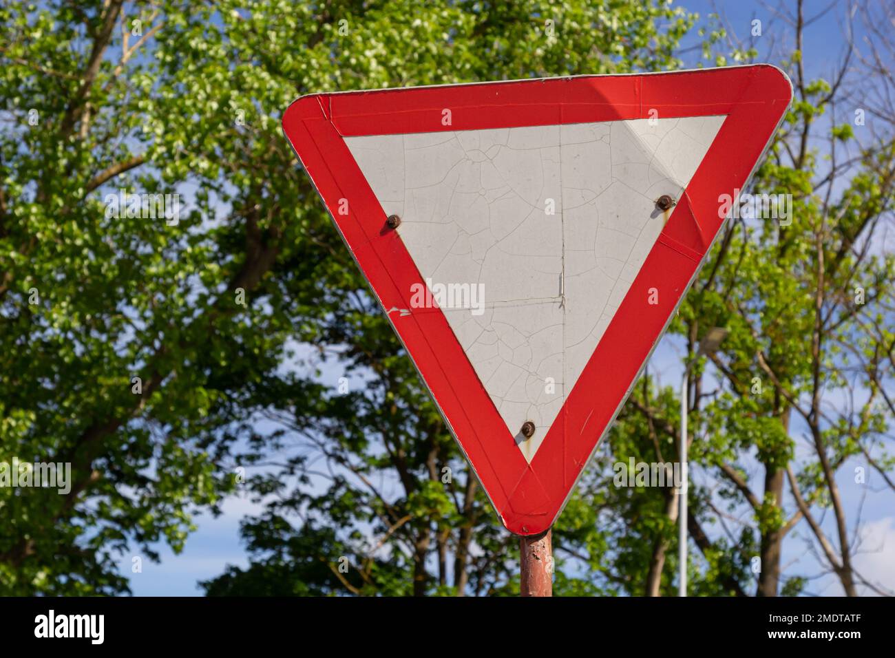 Close-up of give way road sign. Red and white triangle. Green trees and ...