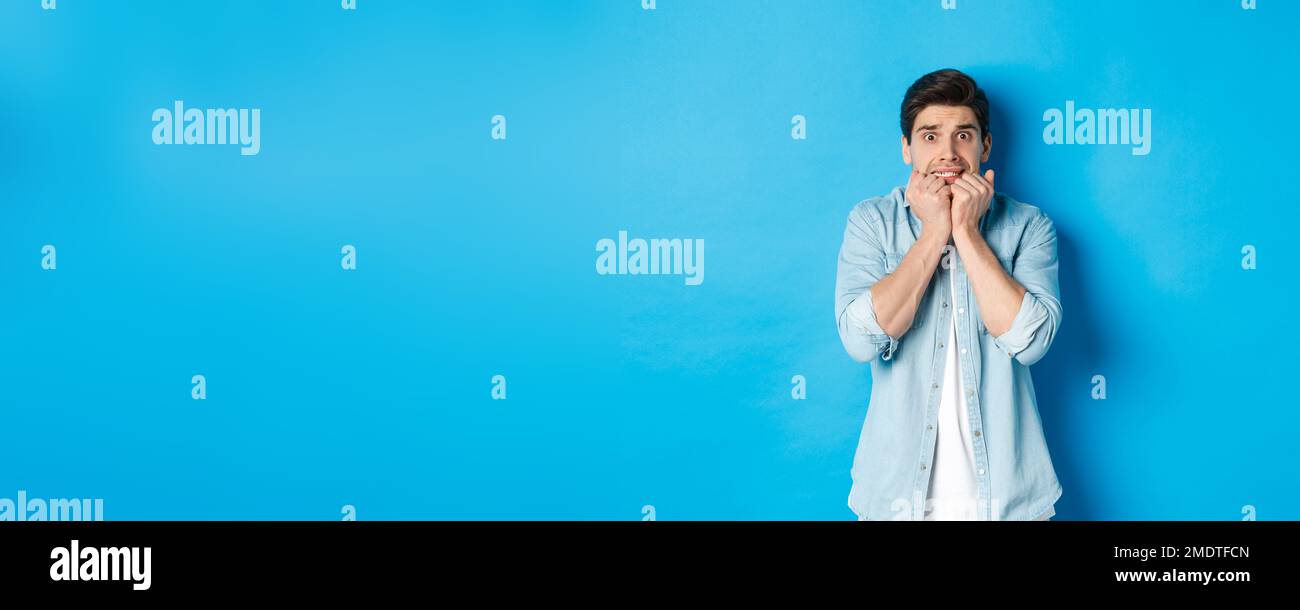 Scared adult man looking at something scary, biting fingernails and ...