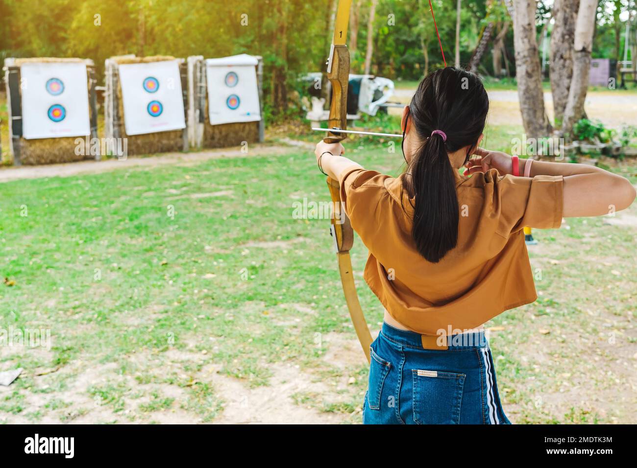 Back view of Asian girl wear face mask aims archery bow and arrow to ...