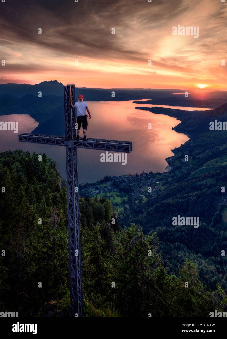 A giant cross on a mountain with a man standing on it during sunset ...