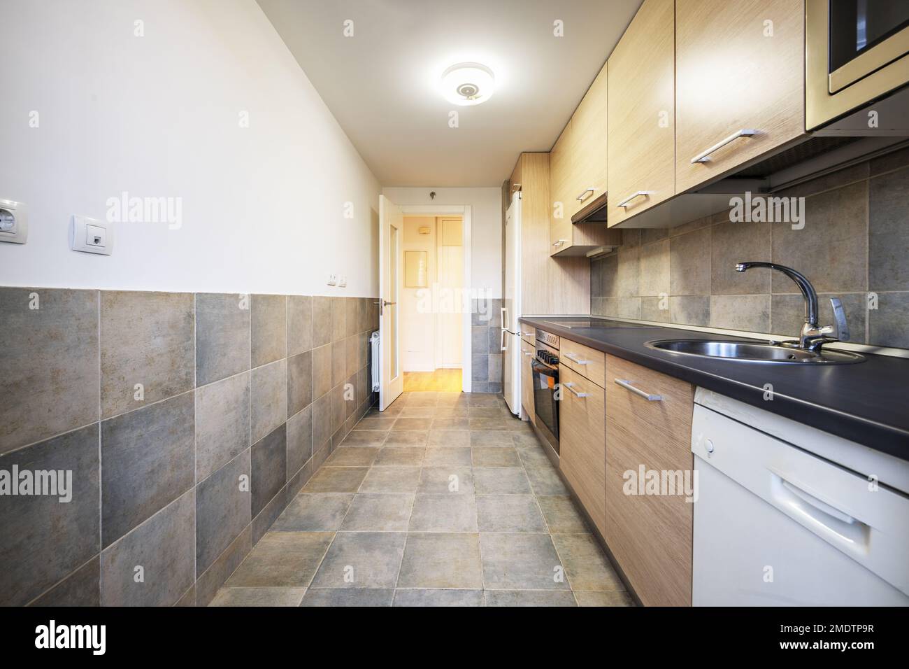 Elongated kitchen with wooden furniture with a black top, gray tiles, a ...