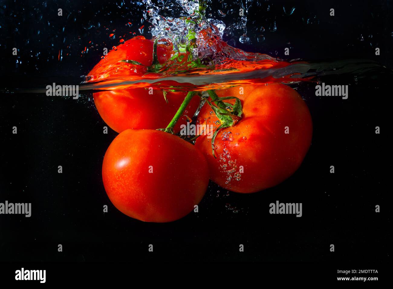 Fresh red tomato falling into water with water splash and air bubbles ...