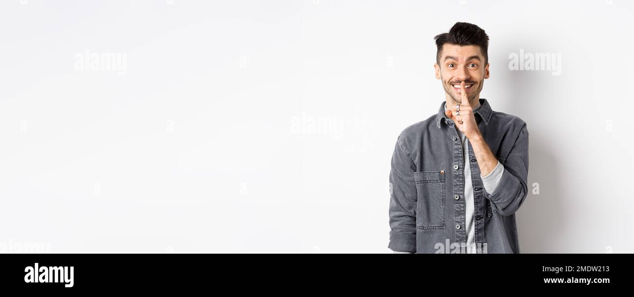 Happy guy shushing at camera, smiling with finger on lips, asking to ...