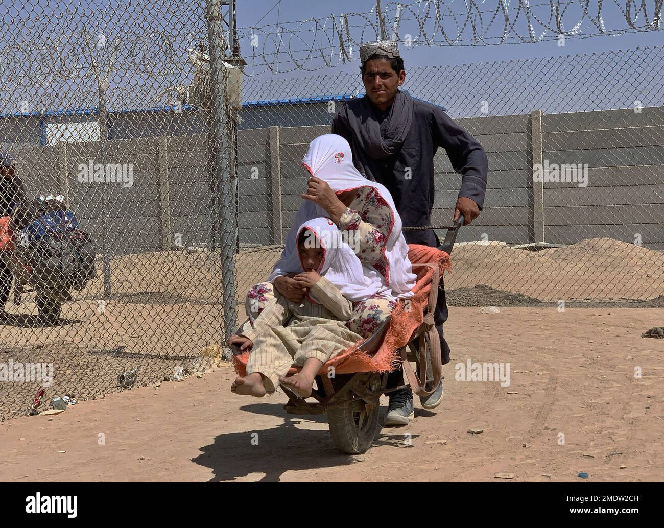 A porter pushes a wheelbarrow carrying an Afghan woman with her son as ...