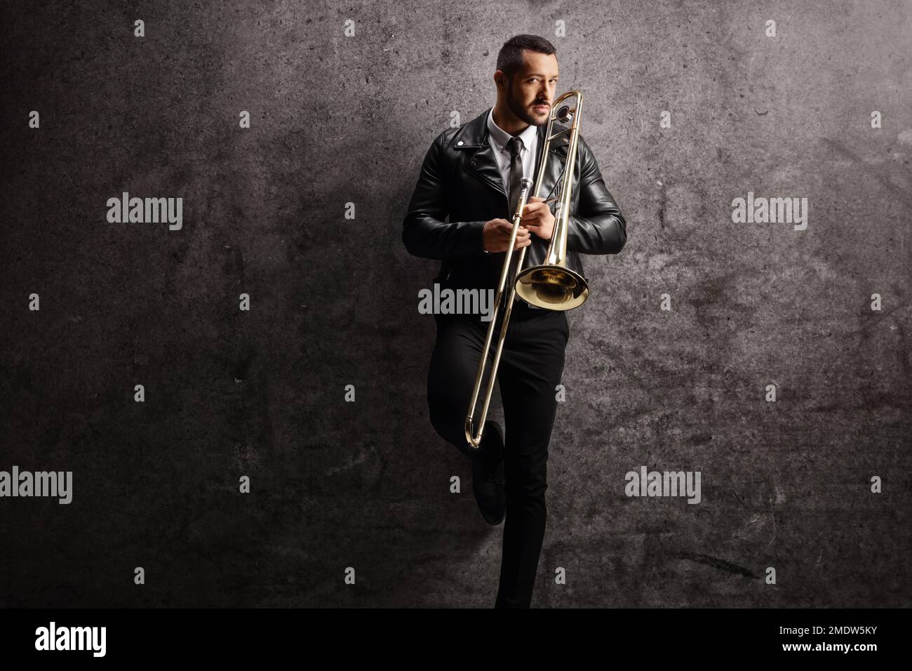 Young man in a leather jacket holding a trombone and standing against a ...