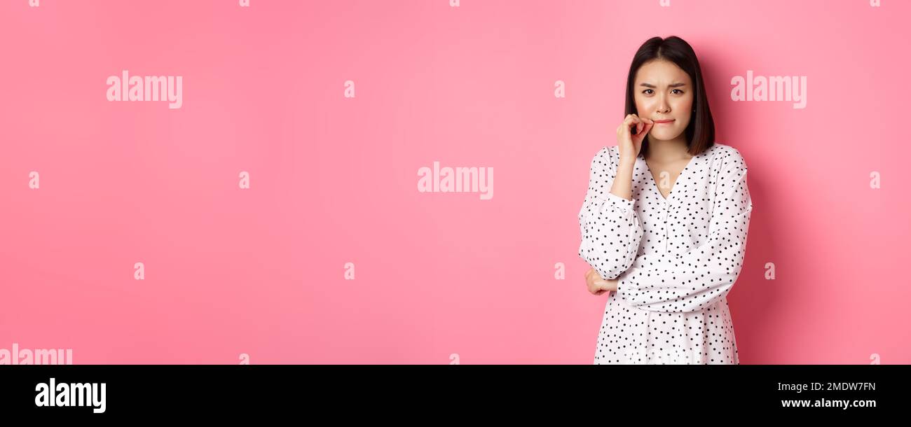 Brunette asian woman in dress looking displeased, frowning and zipping ...