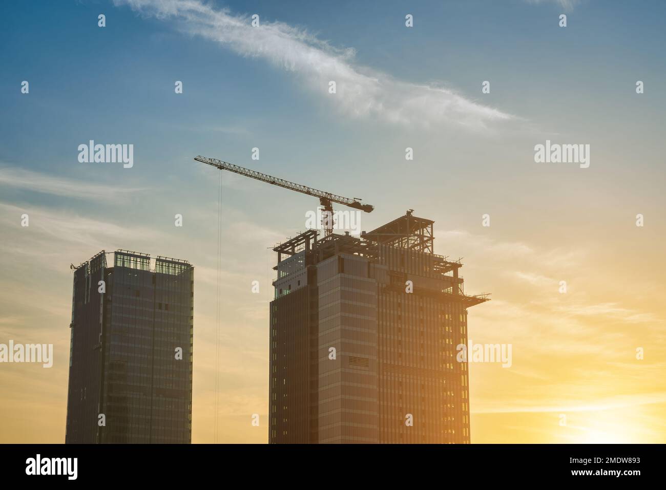 A crane building a modern skyscraper against a sunset. Construction ...