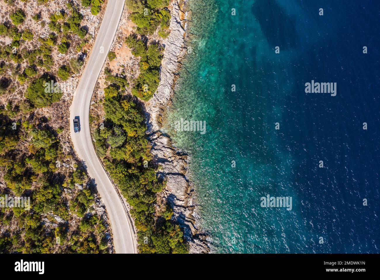 Aerial vertical shot of pickup truck moving by the curved road near sea ...