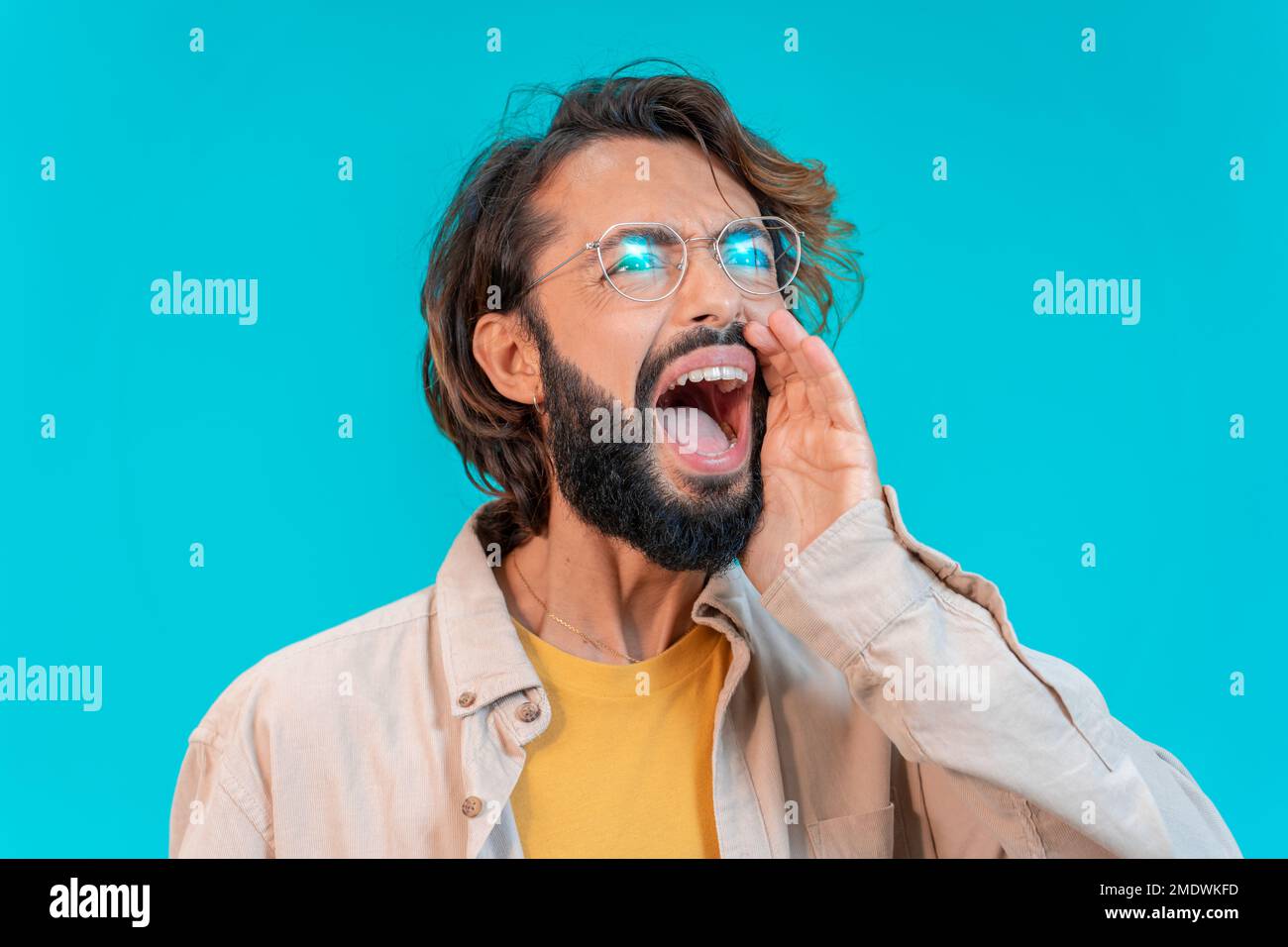 Young man shouting loud calling attention isolated on blue studio ...